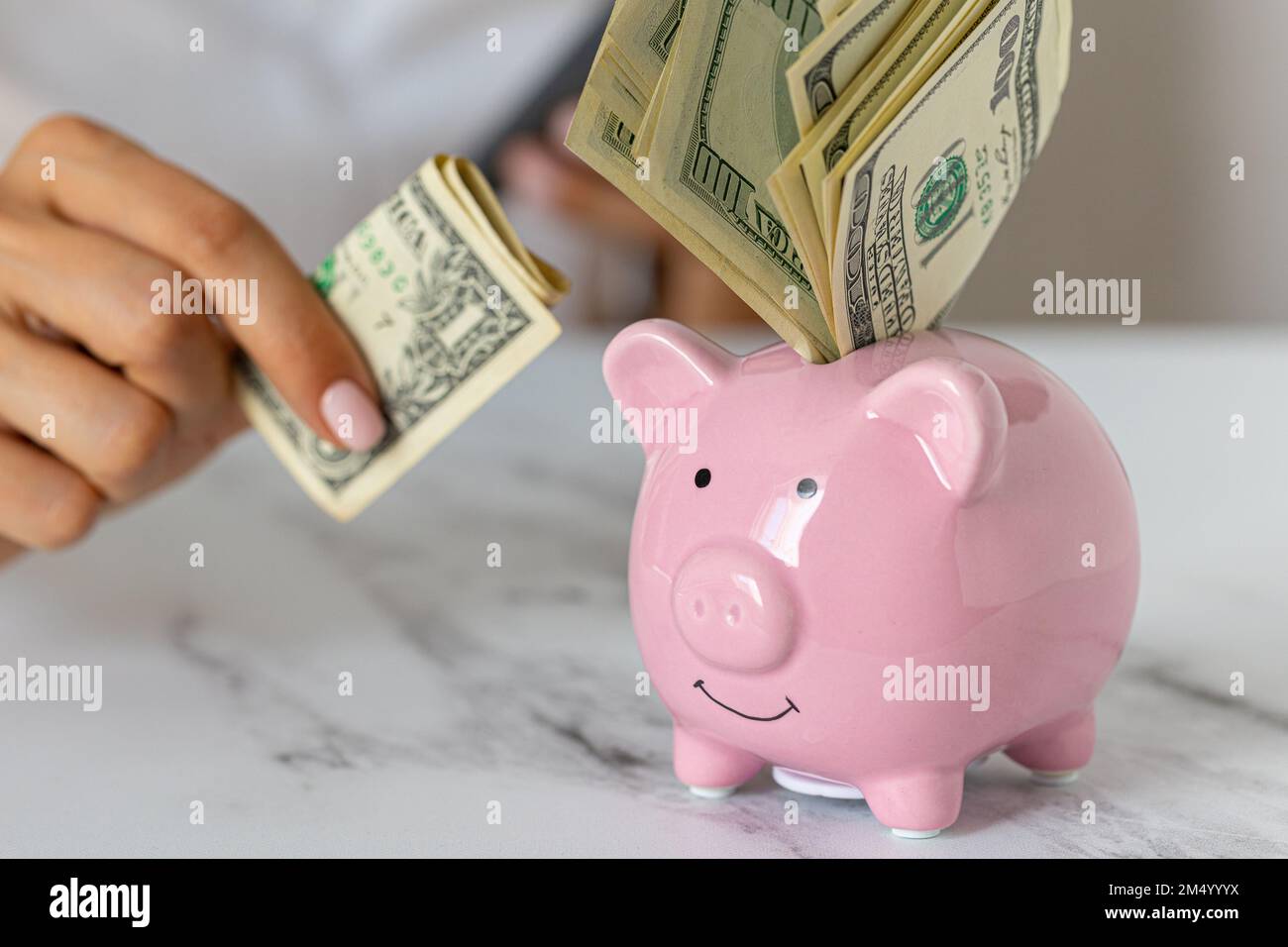 Close-up of a woman's hands put dollar paper money in a piggy bank ...