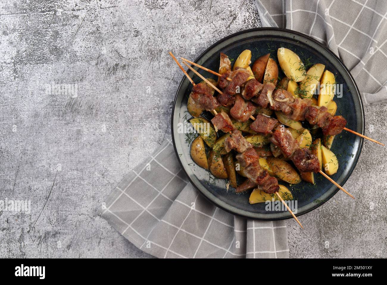 Kebabs on wooden skewers with potatoes and greens on a round plate on a ...