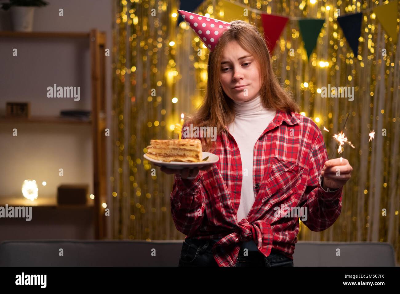 Upset displeased girl at her birthday party holding a cake and ...