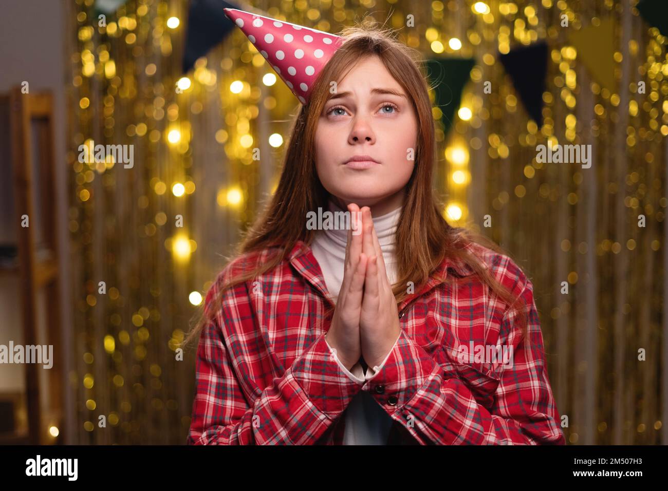 Mournful emotional young girl wearing holiday cap and shirt looking up ...