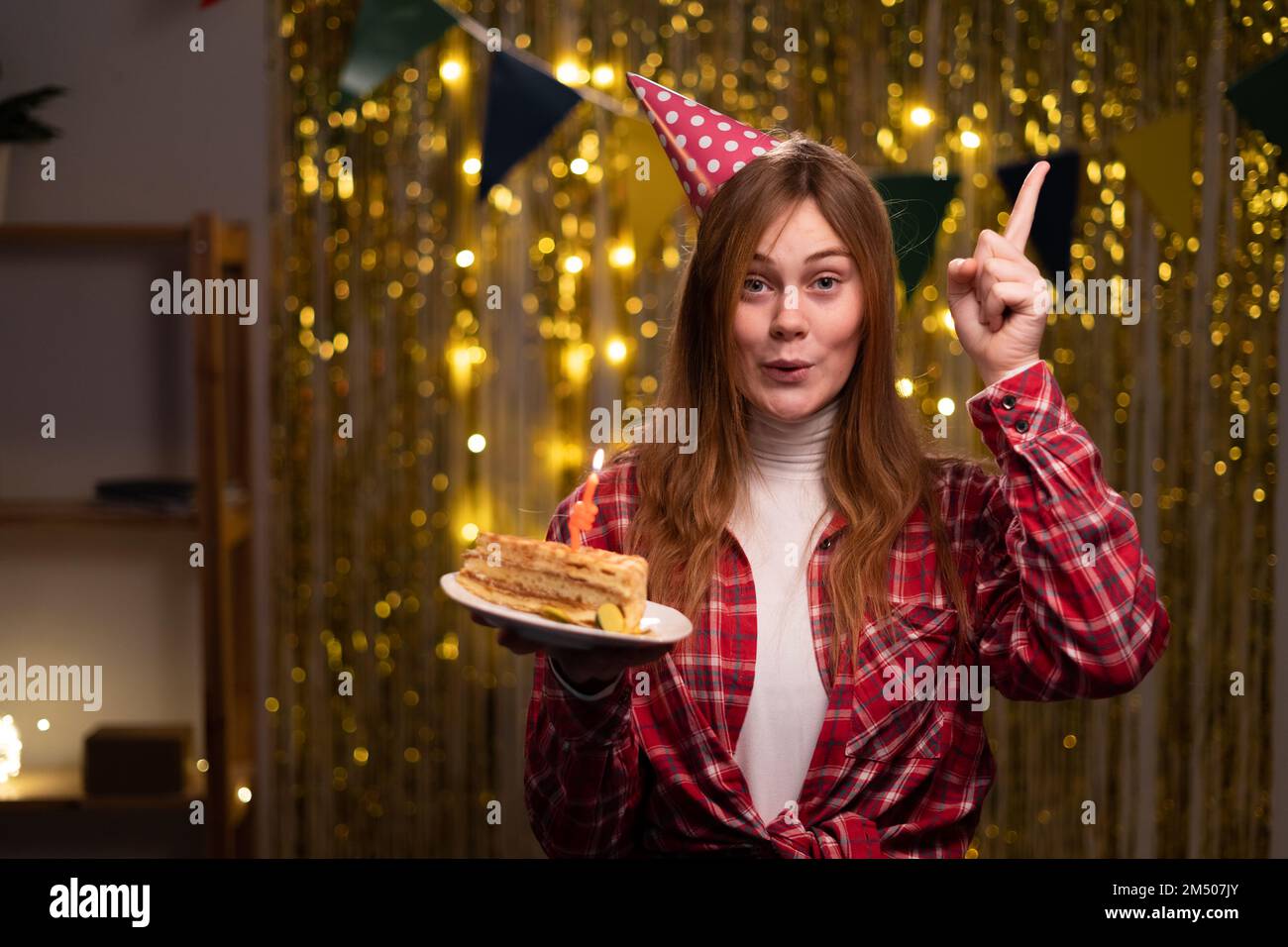 Inspired young woman with a cake at a birthday party standing finger up ...