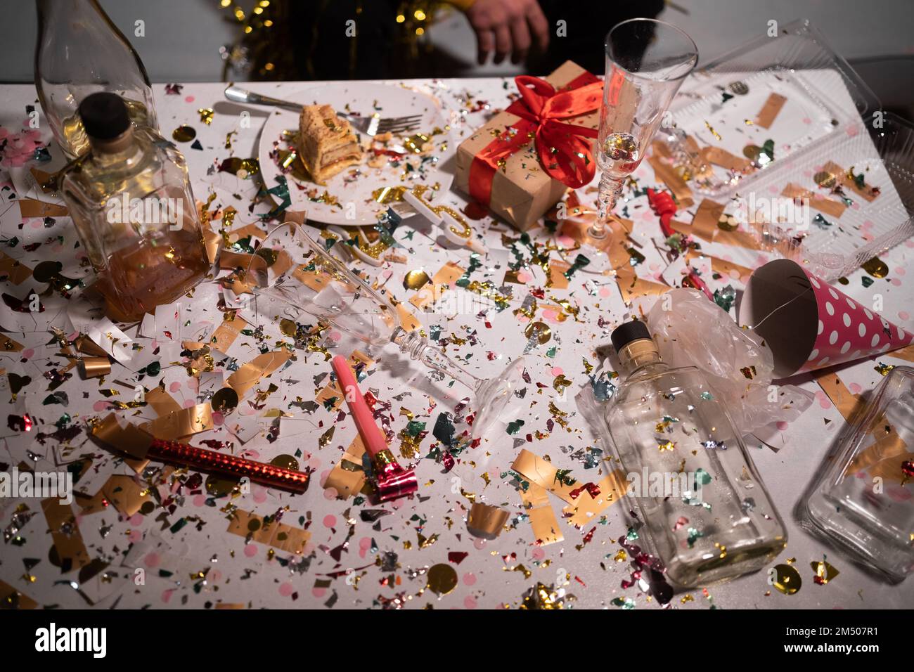 Confetti, empty bottles and party hats on a white table. After party ...