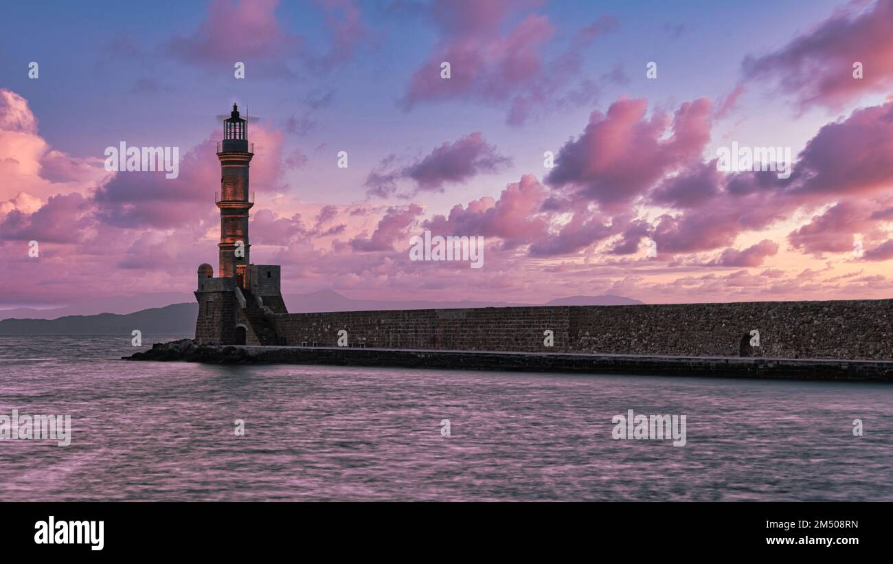 A lighthouse in the middle of a sea under a pink and blue clouded sky ...