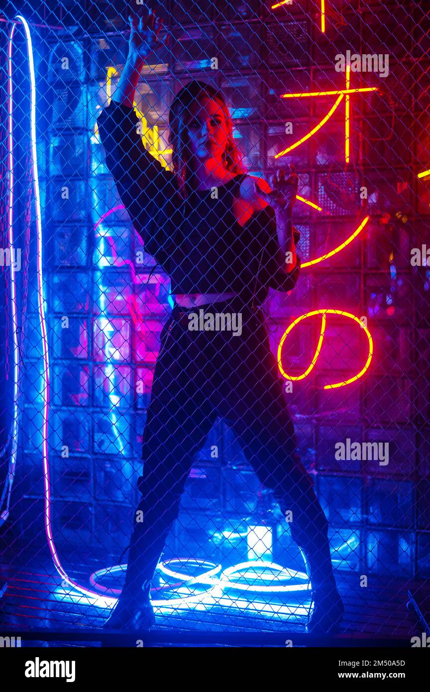 Caucasian woman in neon studio behind chain-link mesh Stock Photo - Alamy