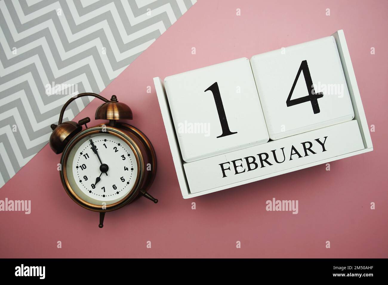 Alarm clock and wooden calendar with date of February 14 on pink ...