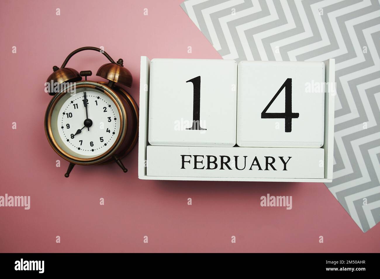 Alarm clock and wooden calendar with date of February 14 on pink ...