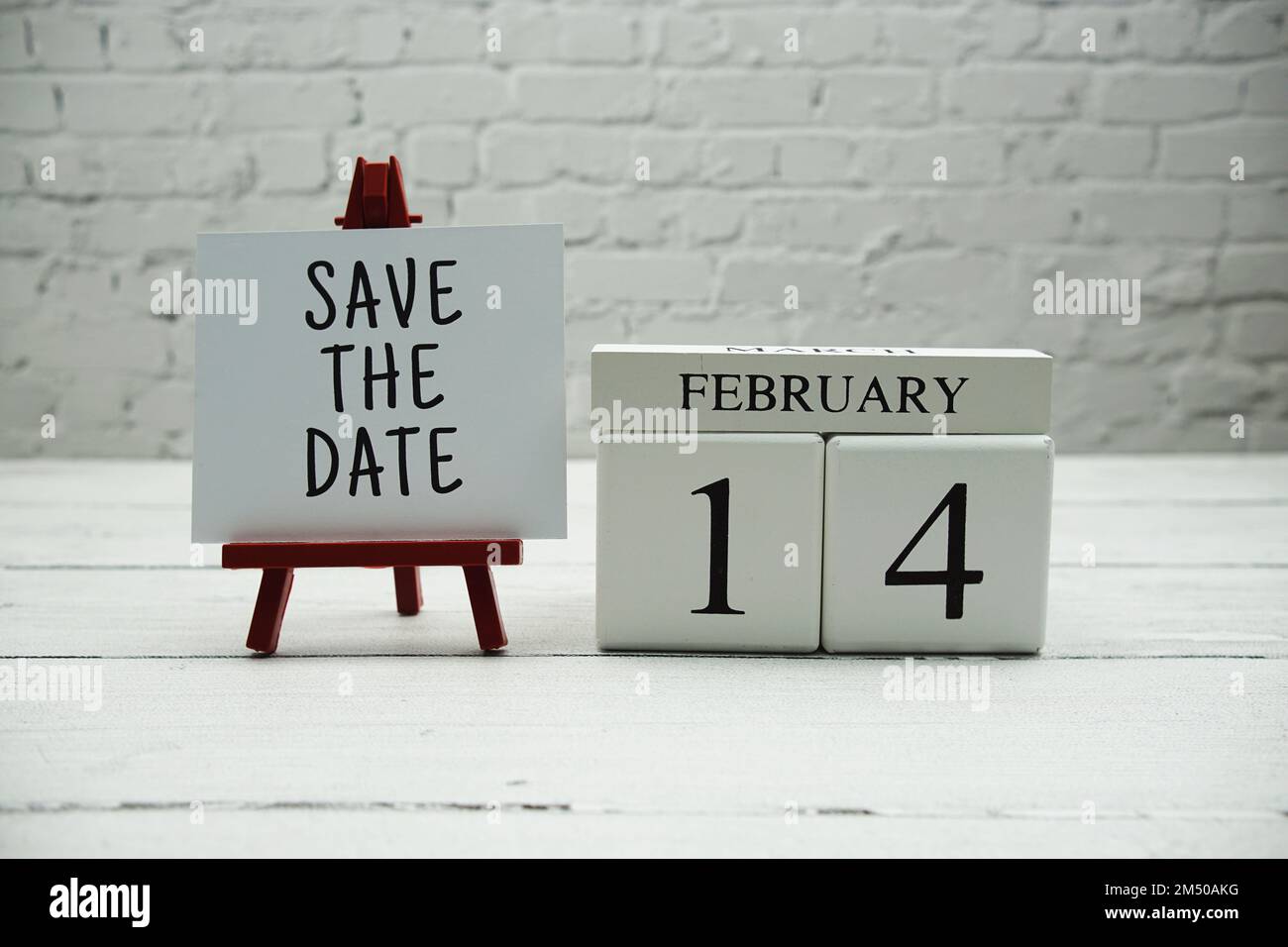14 February Save the Date text on white brick wall and wooden ...