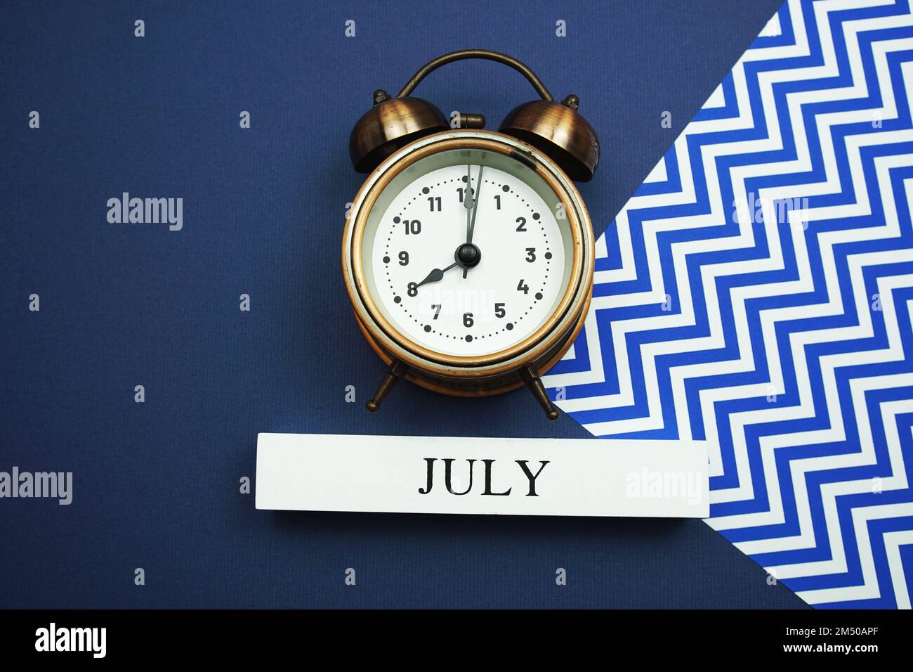 July and alarm clock on navy blue background Stock Photo - Alamy