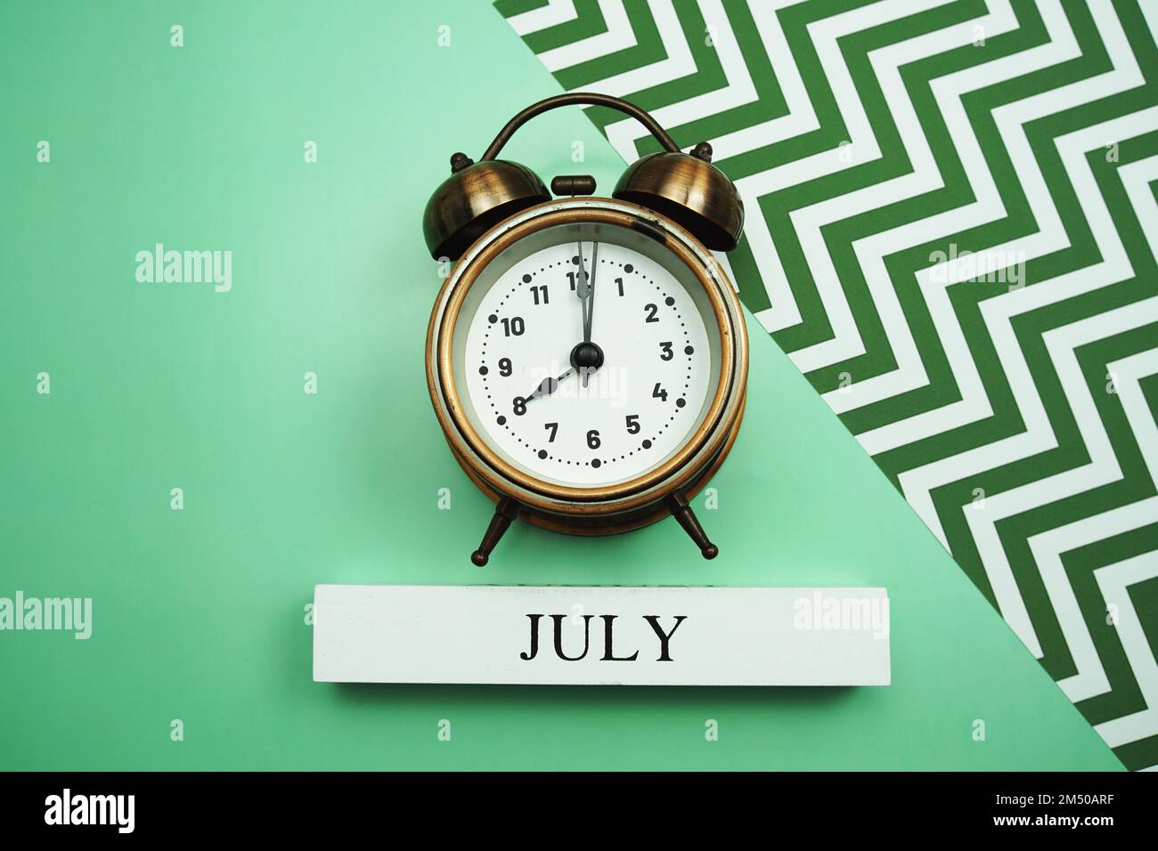 July and alarm clock on green background Stock Photo - Alamy