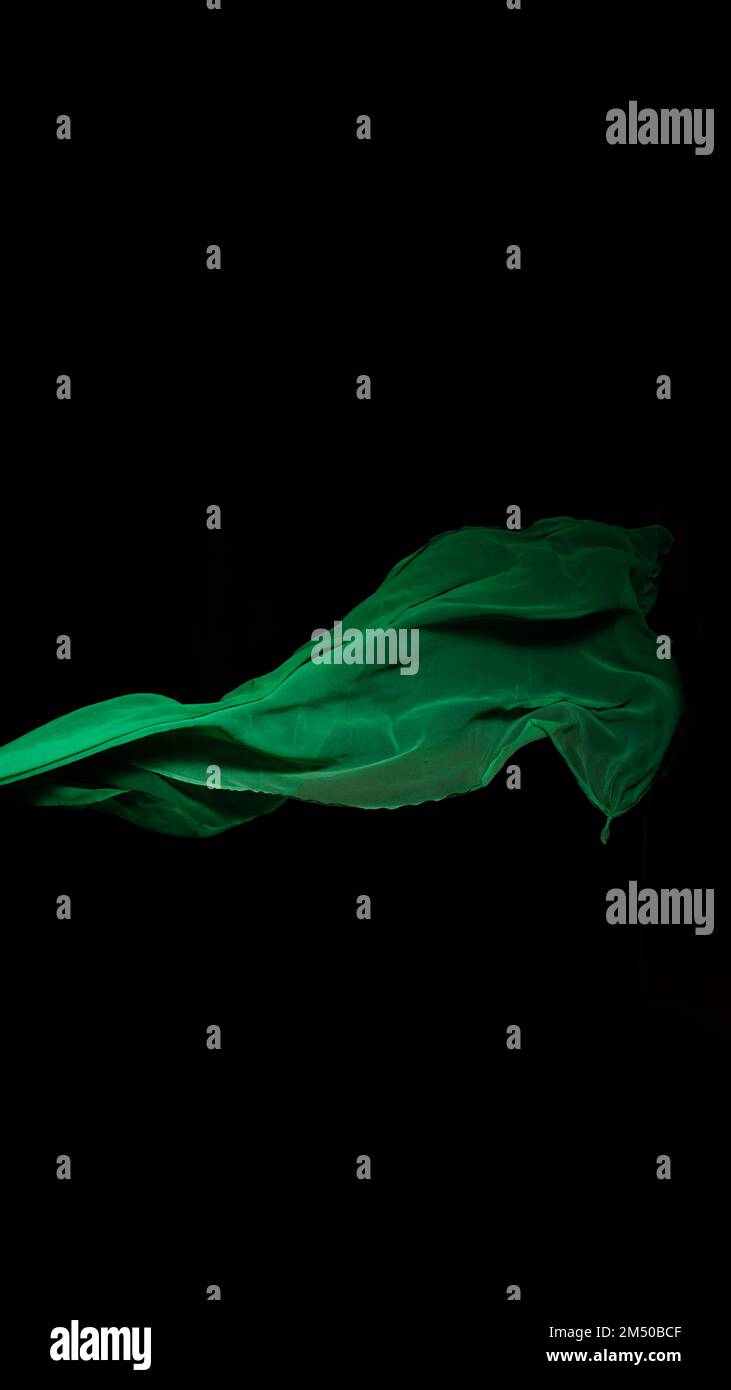 An illuminated green transparent fluttering canvas on a black ...