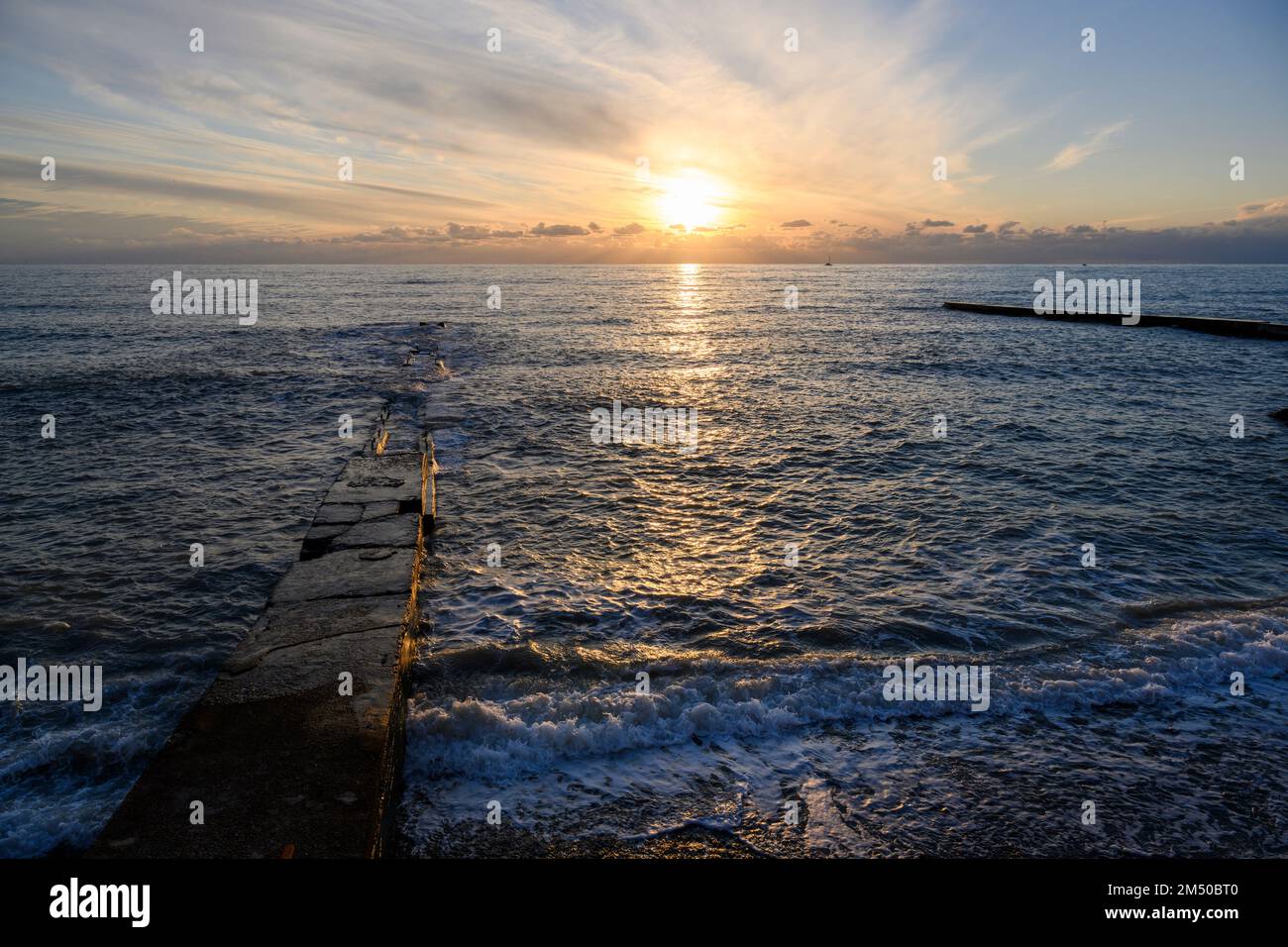 Sunset over the sea with an old breakwater and a yacht on the horizon ...