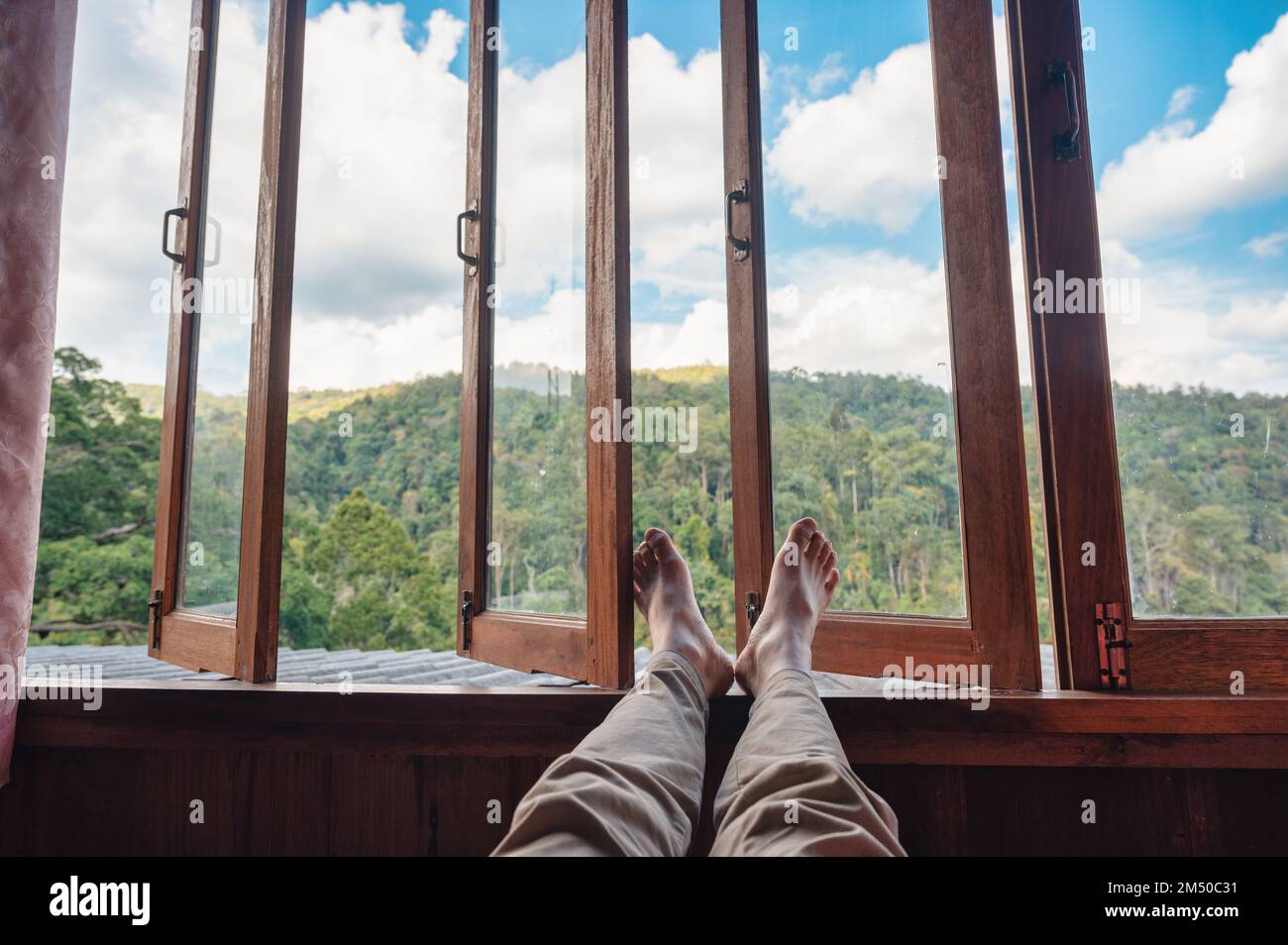 Barefoot man legs relaxing by wooden window in the bedroom and mountain ...