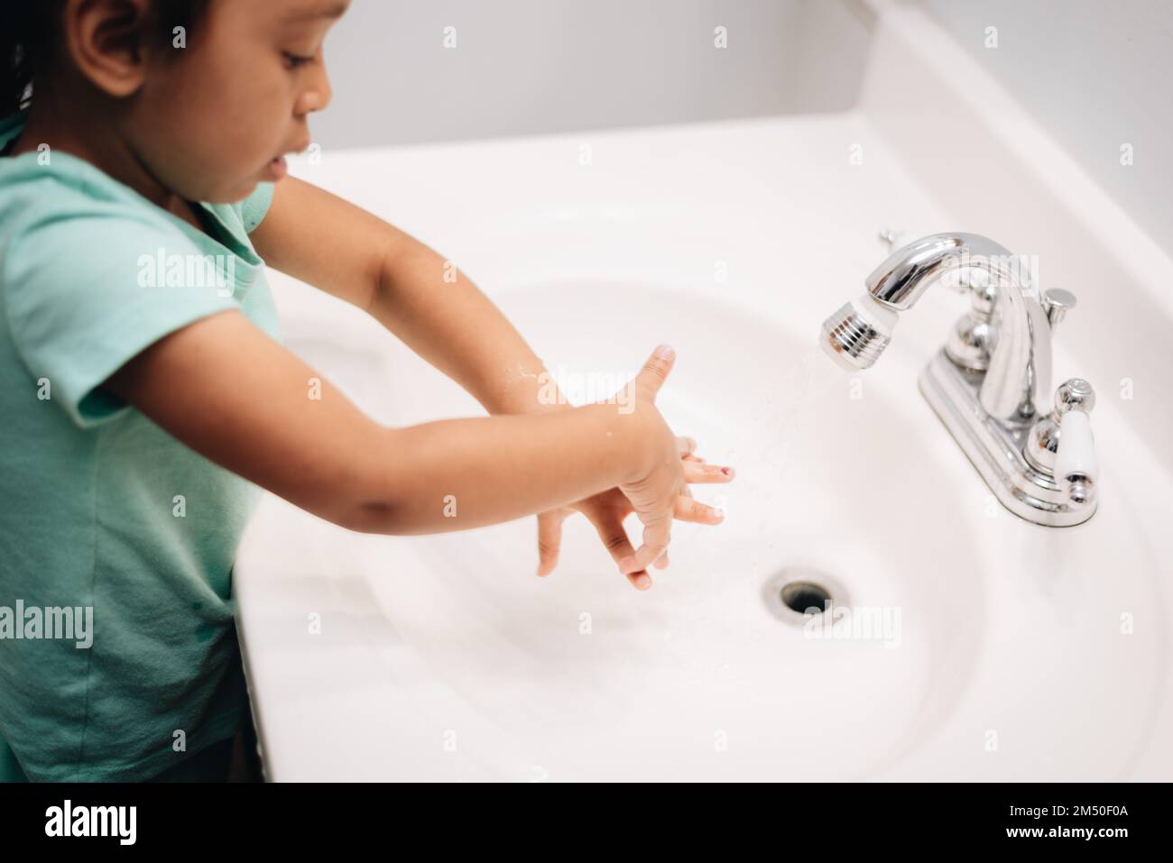 A cute preschool girl practicing good hygiene using the bathroom sink ...