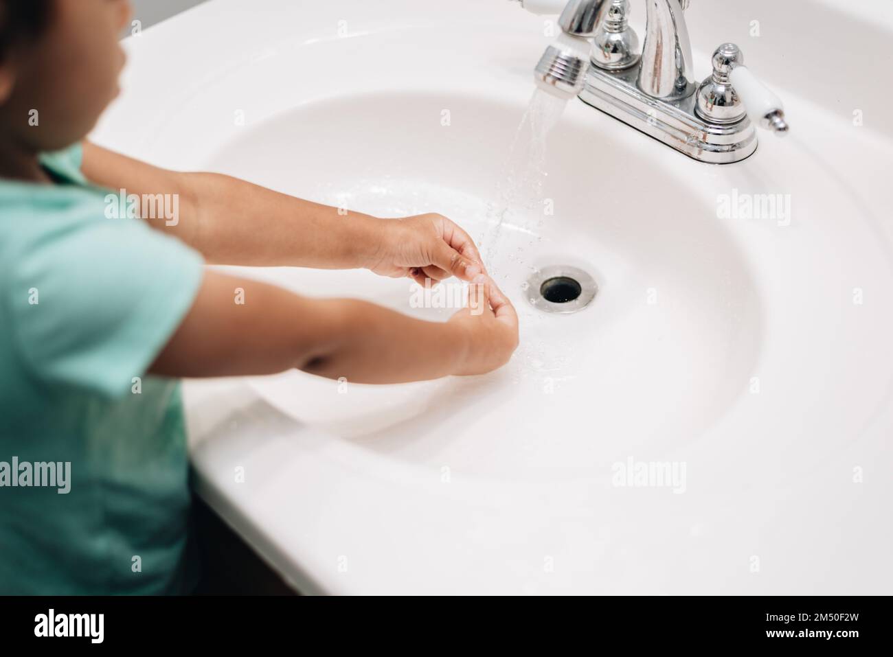 A cute preschool girl practicing good hygiene using the bathroom sink ...