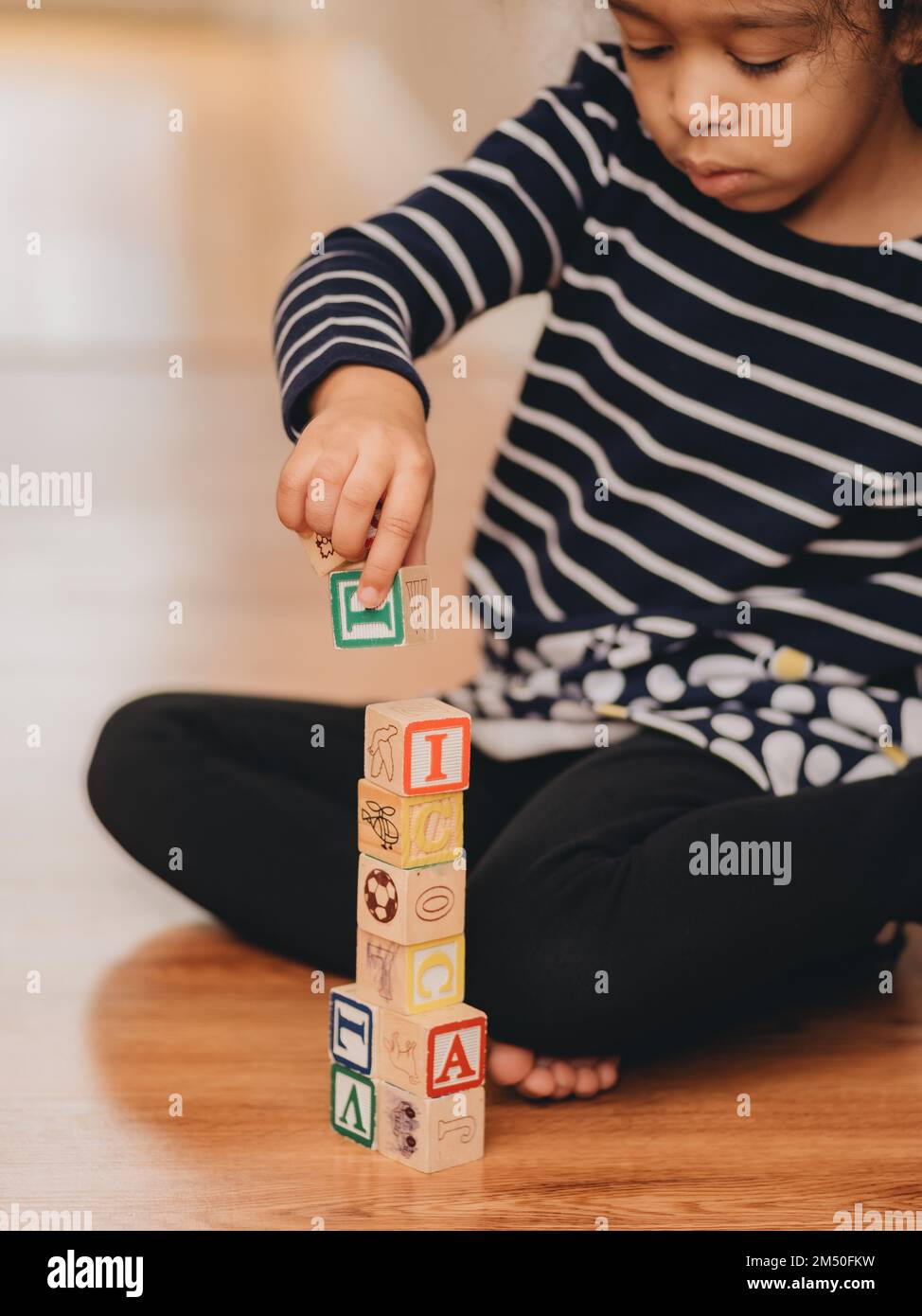 A preschool girl, playing with wooden letter blocks at home on the ...