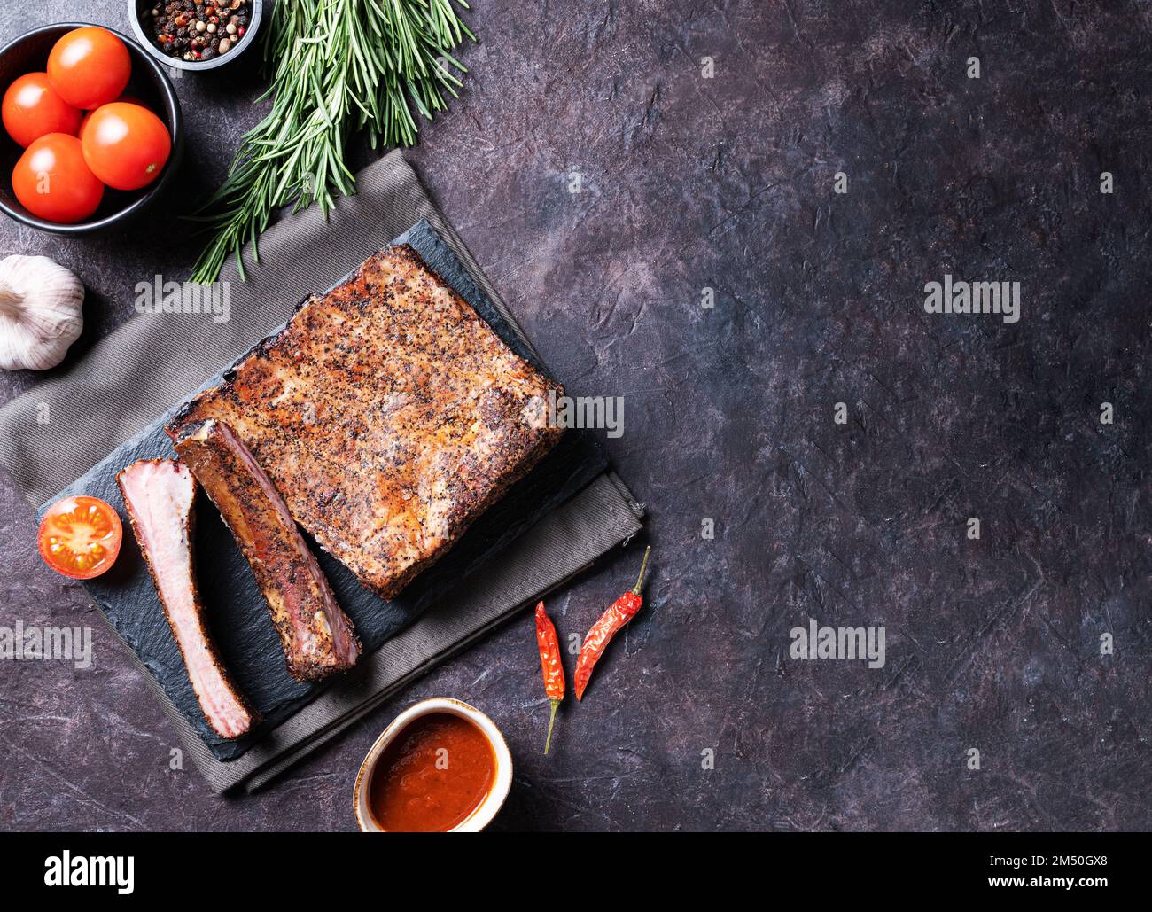 Juicy barbecue pork ribs with tomatoes, sauce and fresh herbs on a dark ...