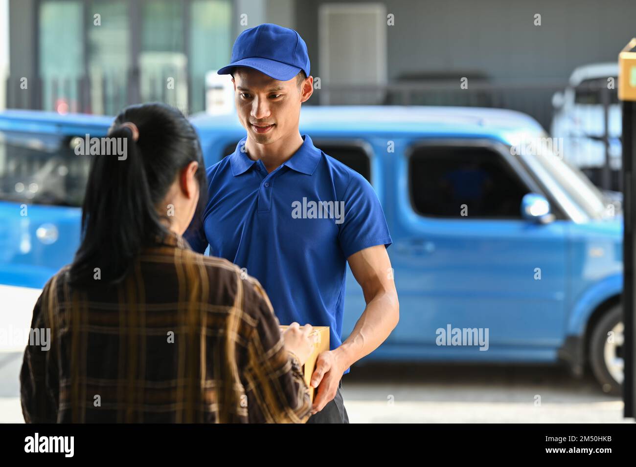 Friendly delivery man giving a cardboard box to woman customer at home ...