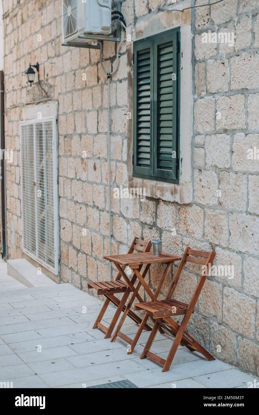 A vertical shot of a stone wall of a house and a wooden folding table ...