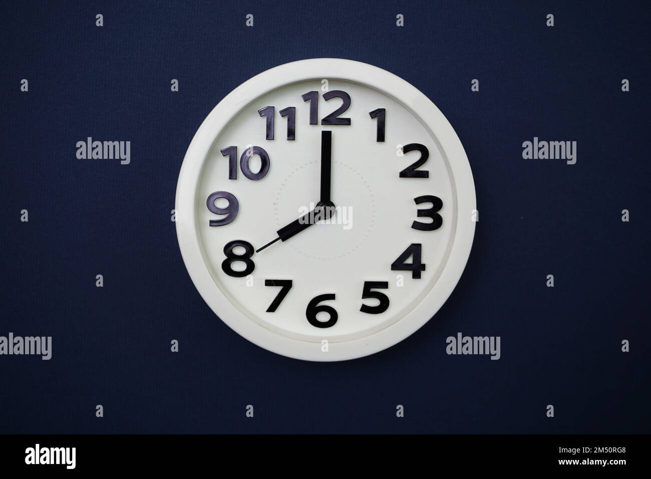 White round clock showing eight o'clock on blue background Stock Photo ...