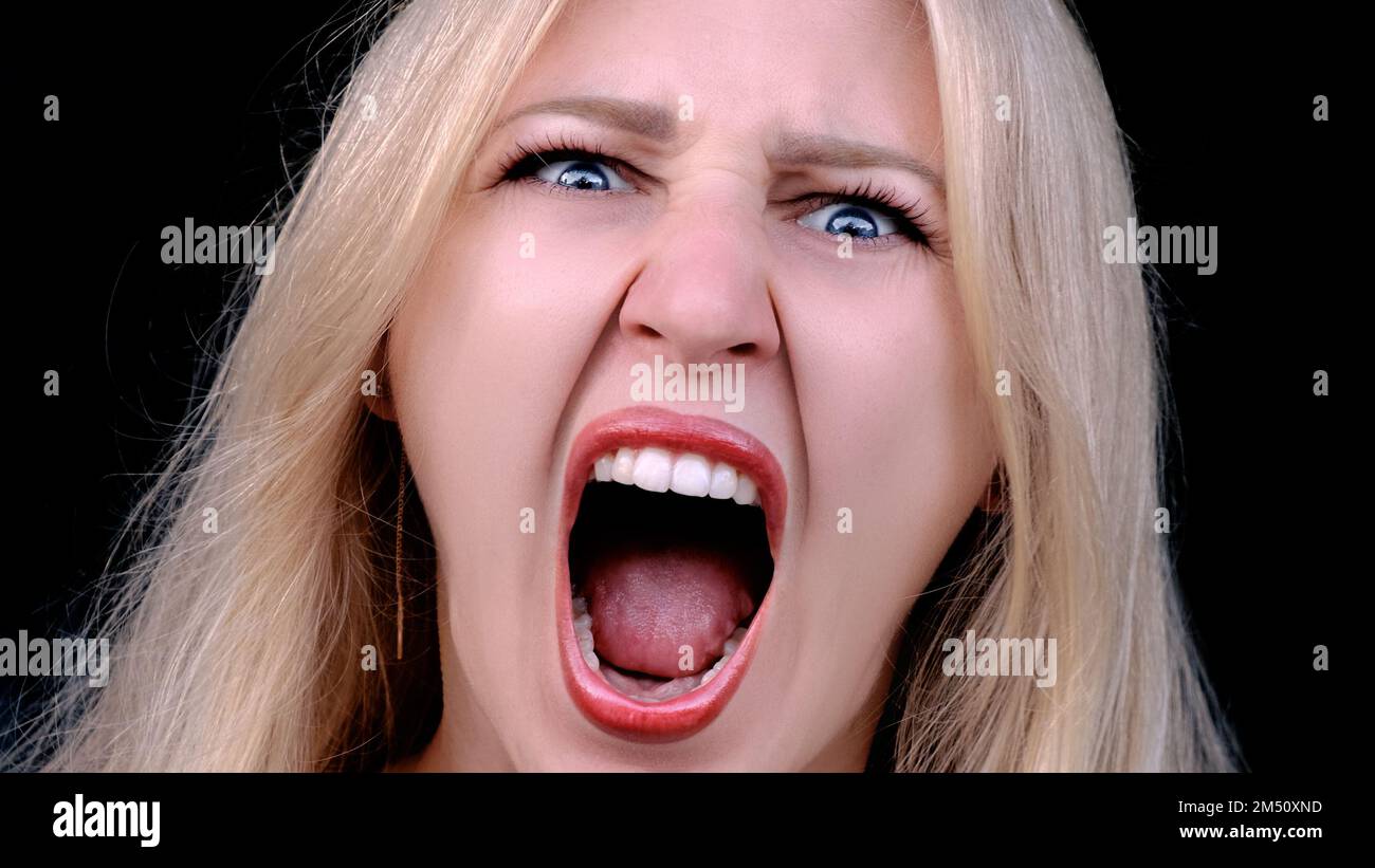 Angry woman yells in rage as she looking at camera on black background ...