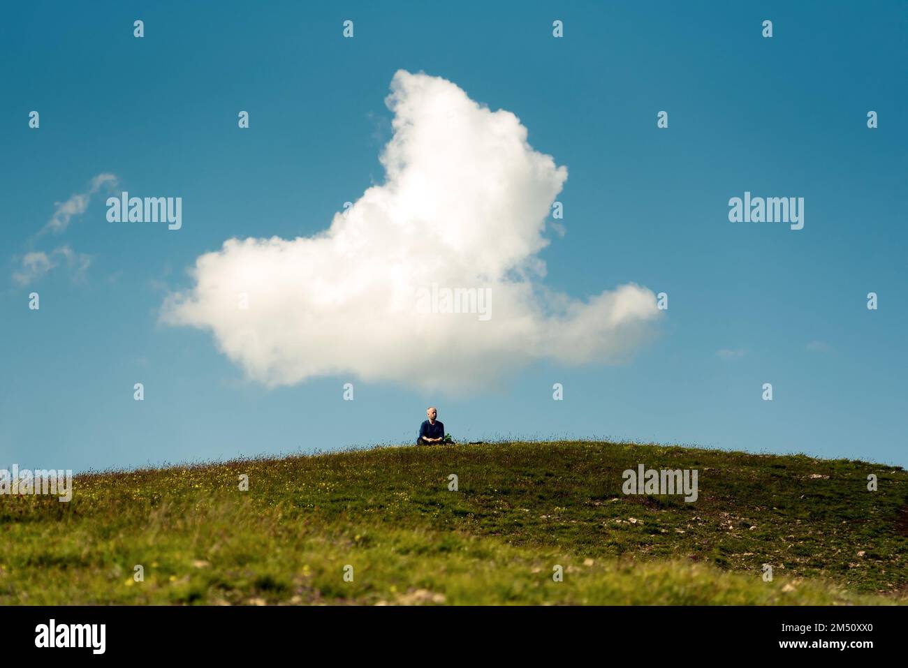 Man sitting on a hill against sky with bird shaped cloud Stock Photo ...
