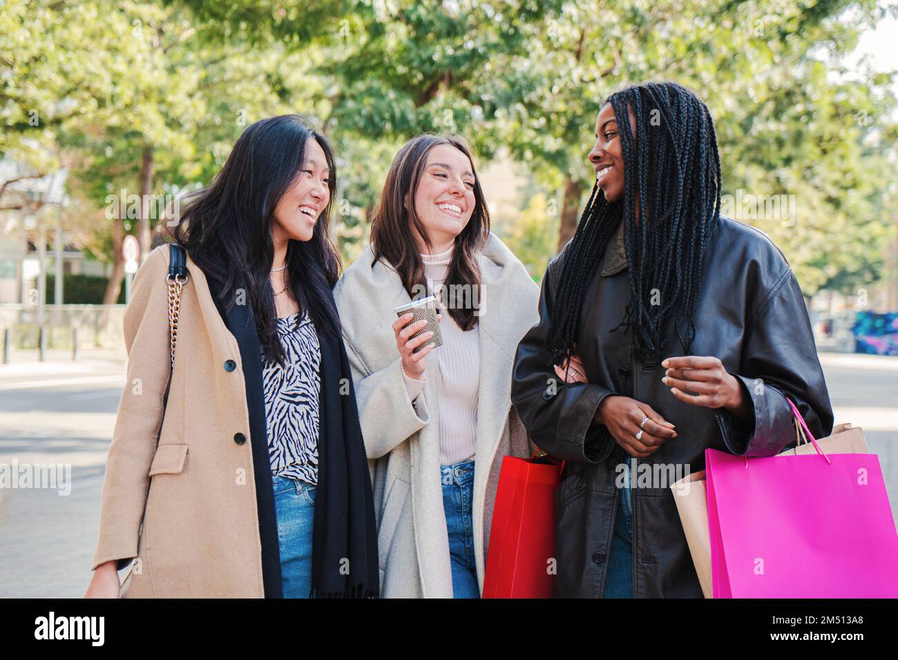 Three multiracial happy young women walking and talking on a shopping ...