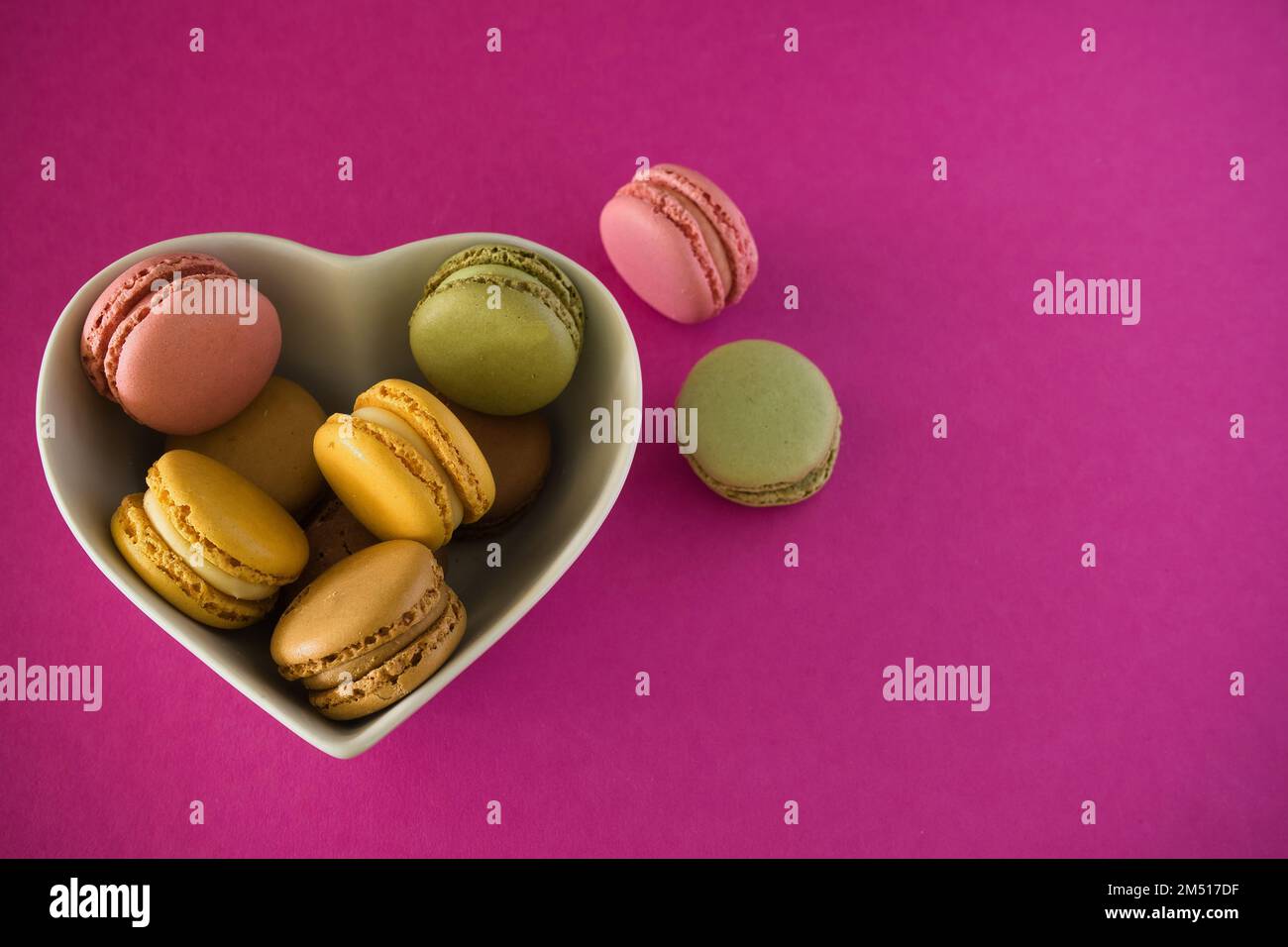 A gift with colorful macaroons inside a heart-shaped box on a hot pink ...
