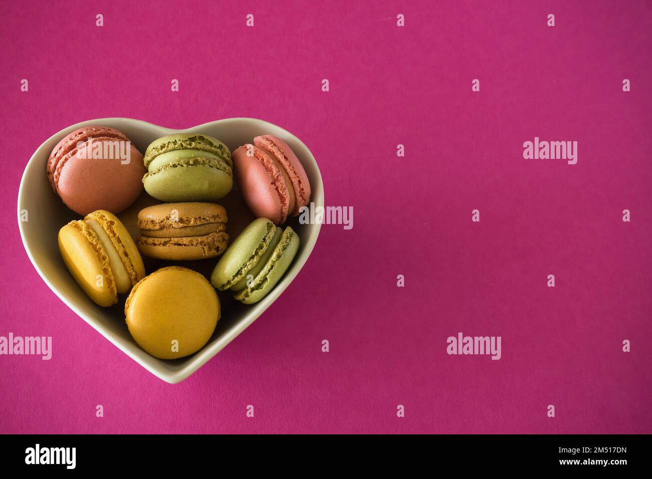 A gift with colorful macaroons inside a heart-shaped box on a hot pink ...