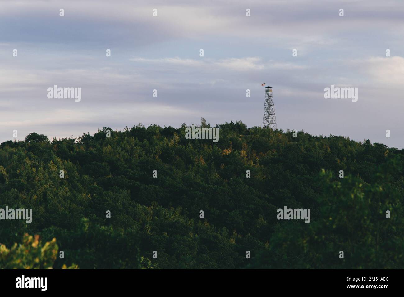 An observation tower with the USA flag on top of the hill with a dense green forest against the ...