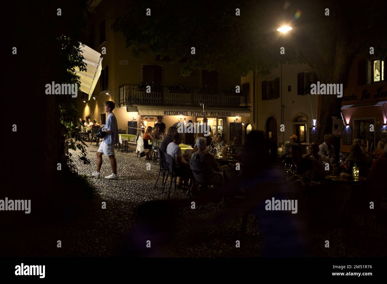 Square with restaurant and people dining at night Stock Photo - Alamy