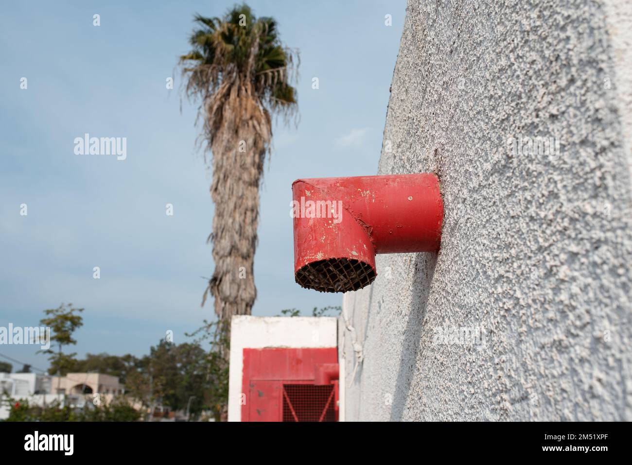 White wall with red pipe and red door.Palm tree and blue sky in the ...