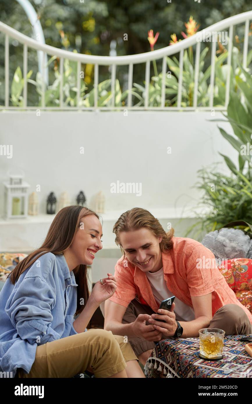 Happy man showing new meme on smartphone screen to laughing girlfriend ...