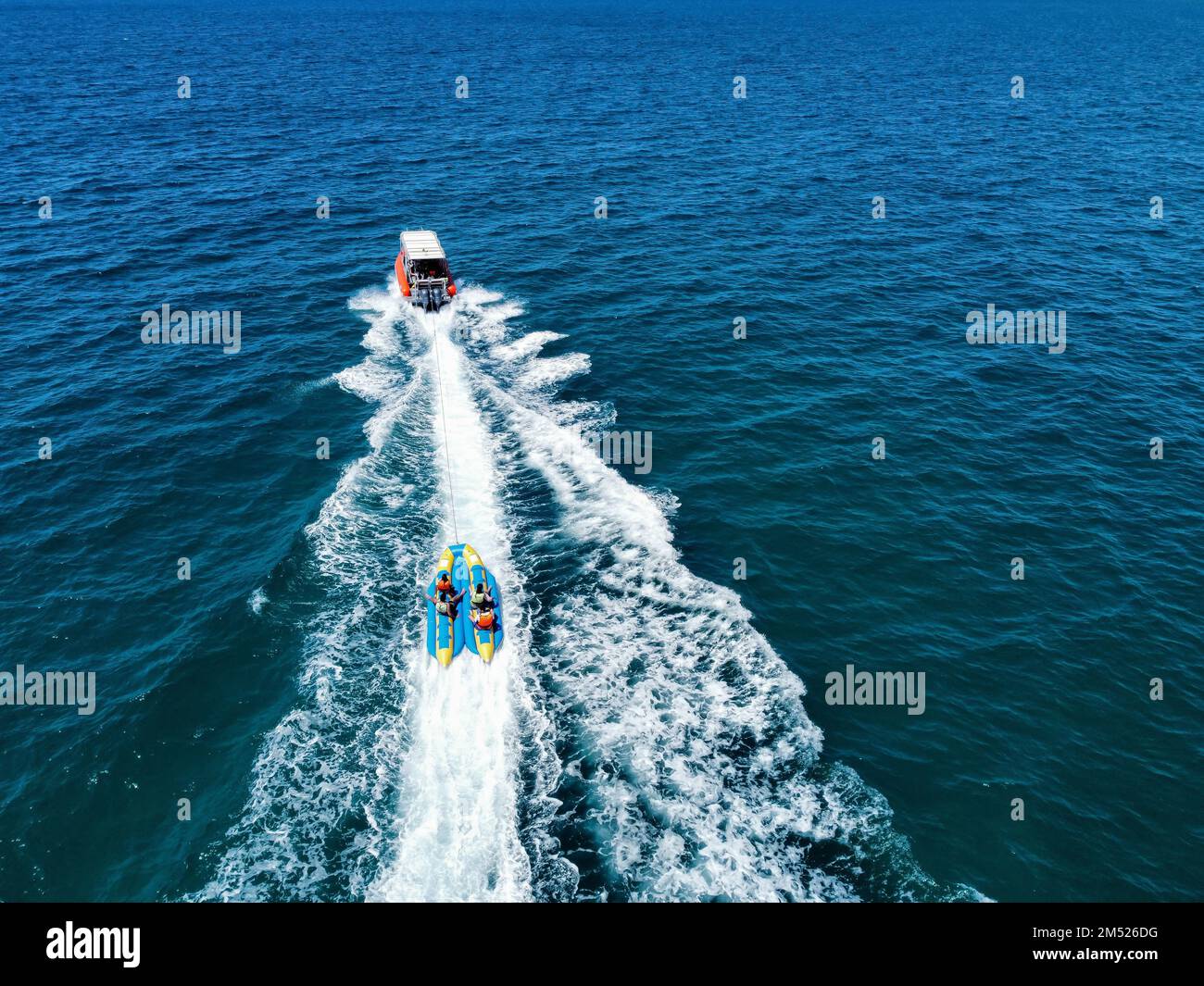A top view of a yacht and people on a banana boat floating on the sea ...