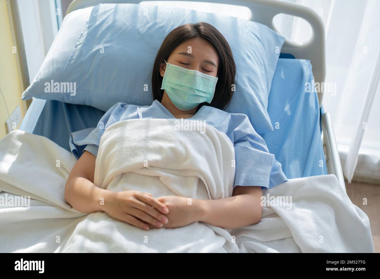 Sad Asian patient woman lying on the hospital bed and wearing a face mask to protect coronavirus ...