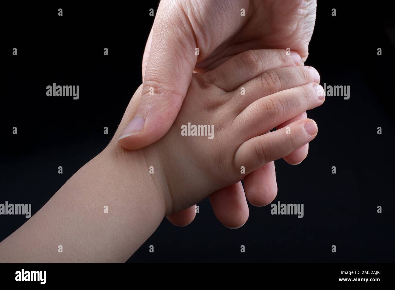 Adult and child hold hands in black background Stock Photo - Alamy