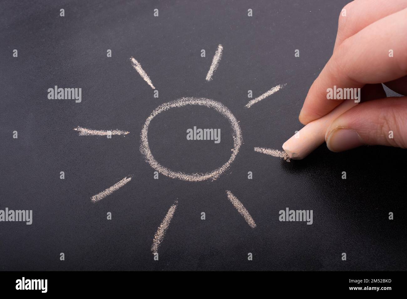 Hand drawing sun by chalk with light ray shape on blackboard background ...