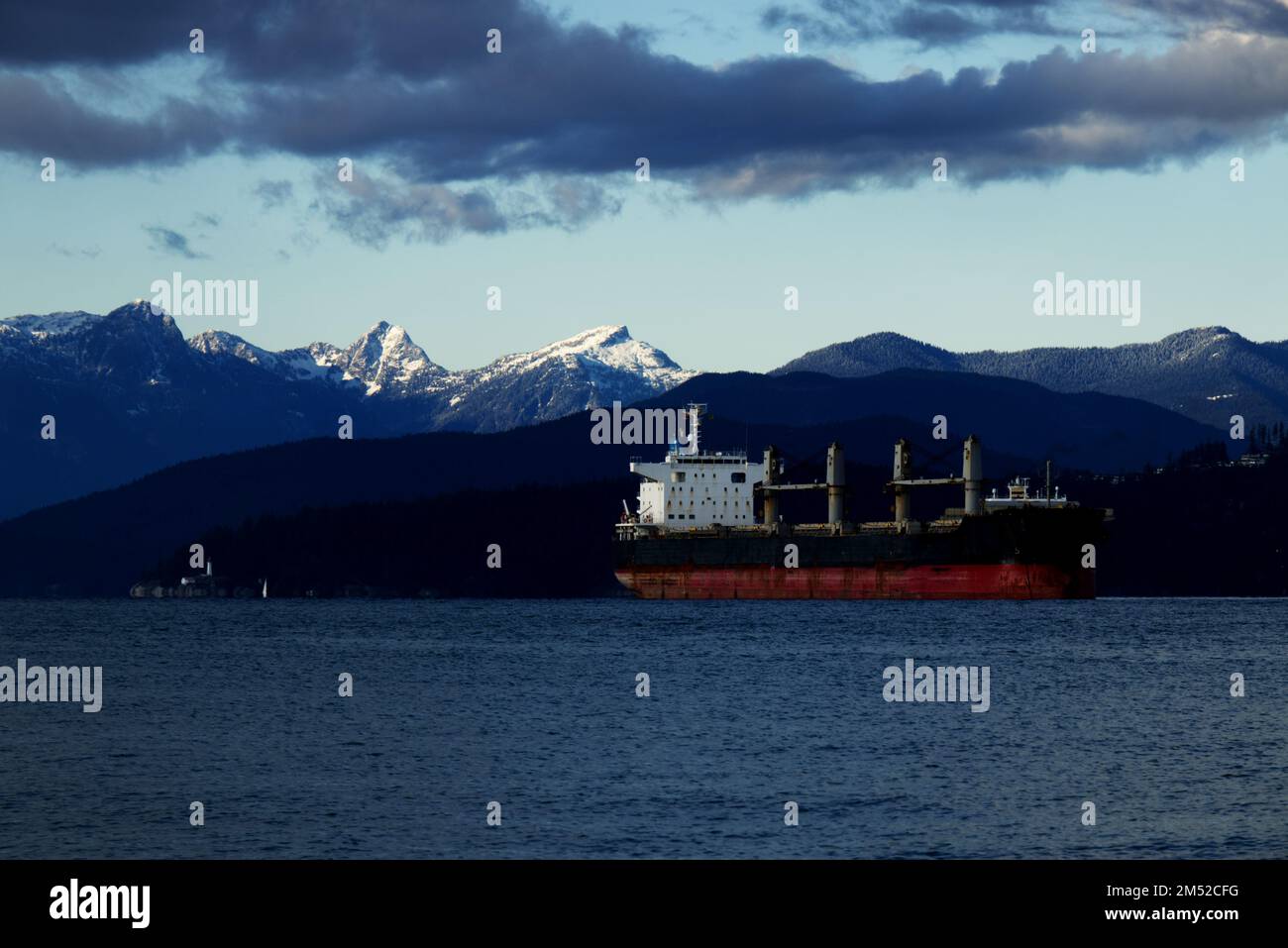 Cargo ship in front of mountains with snow peaks and dramatic clouds ...