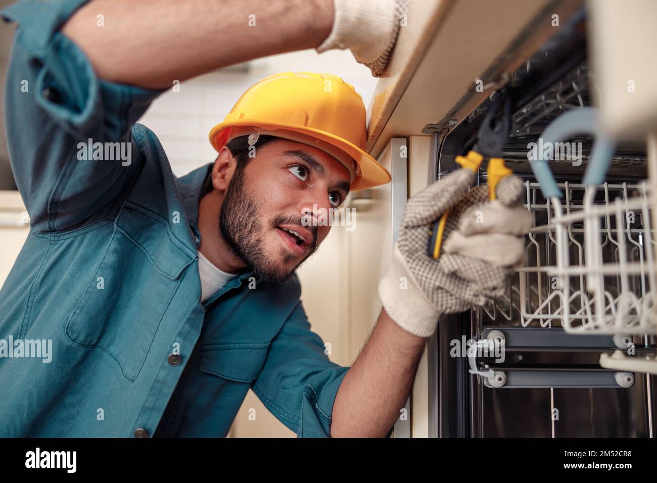 Close up of handyman in special clothing repairing dishwasher in modern ...