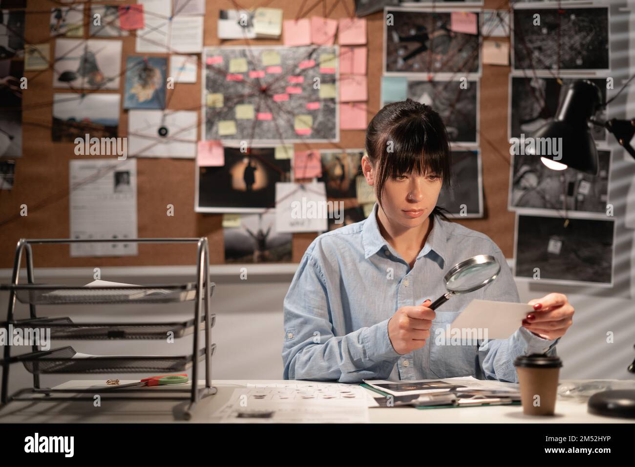 Detective holding magnifying glass in front of photos from murder scene ...