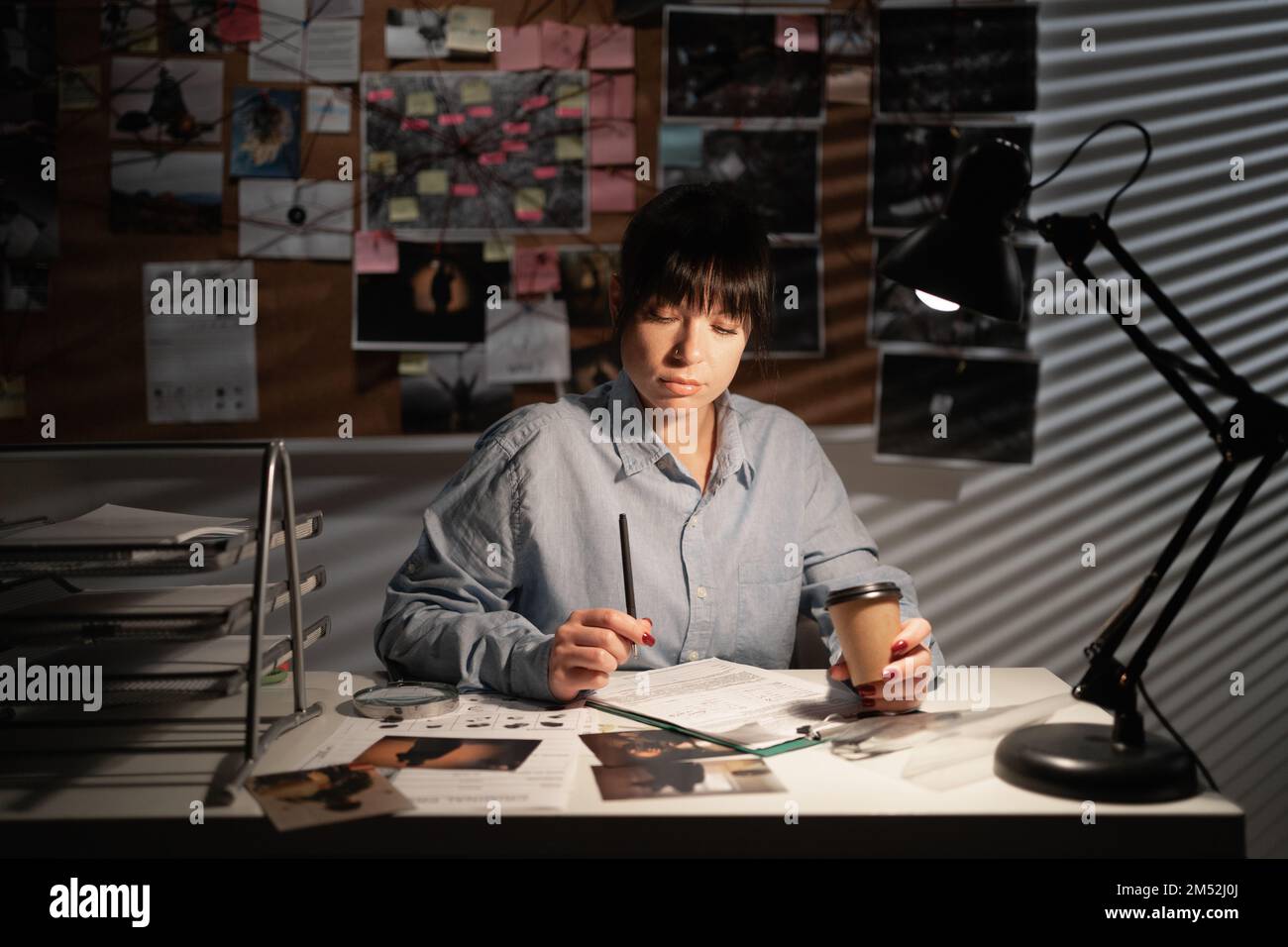 Female detective working in her office drinking coffee and thinking ...