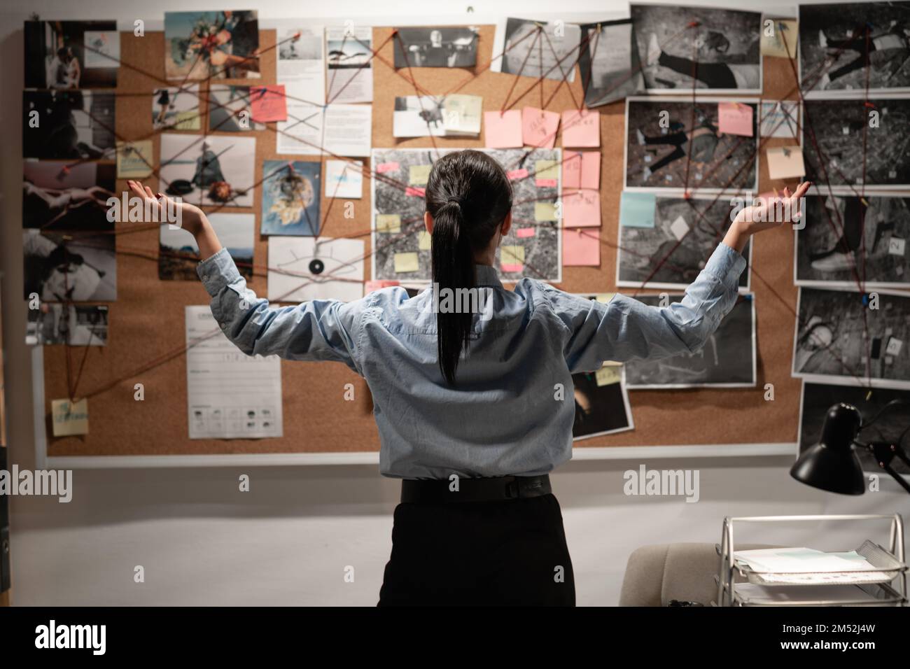 Detective looking at evidence board in office meditation with hands up, back view. Copy space ...