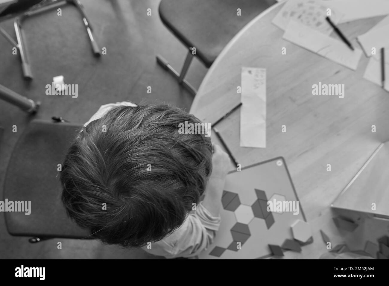 overhead view of a young boy working on arranging shapes into an object ...