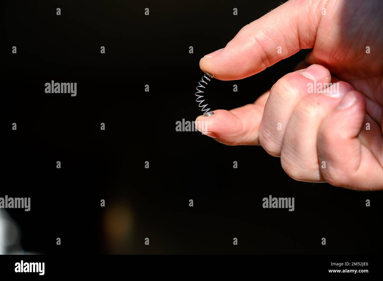 Caucasian hand compressing a metal spring between a thumb and finger ...