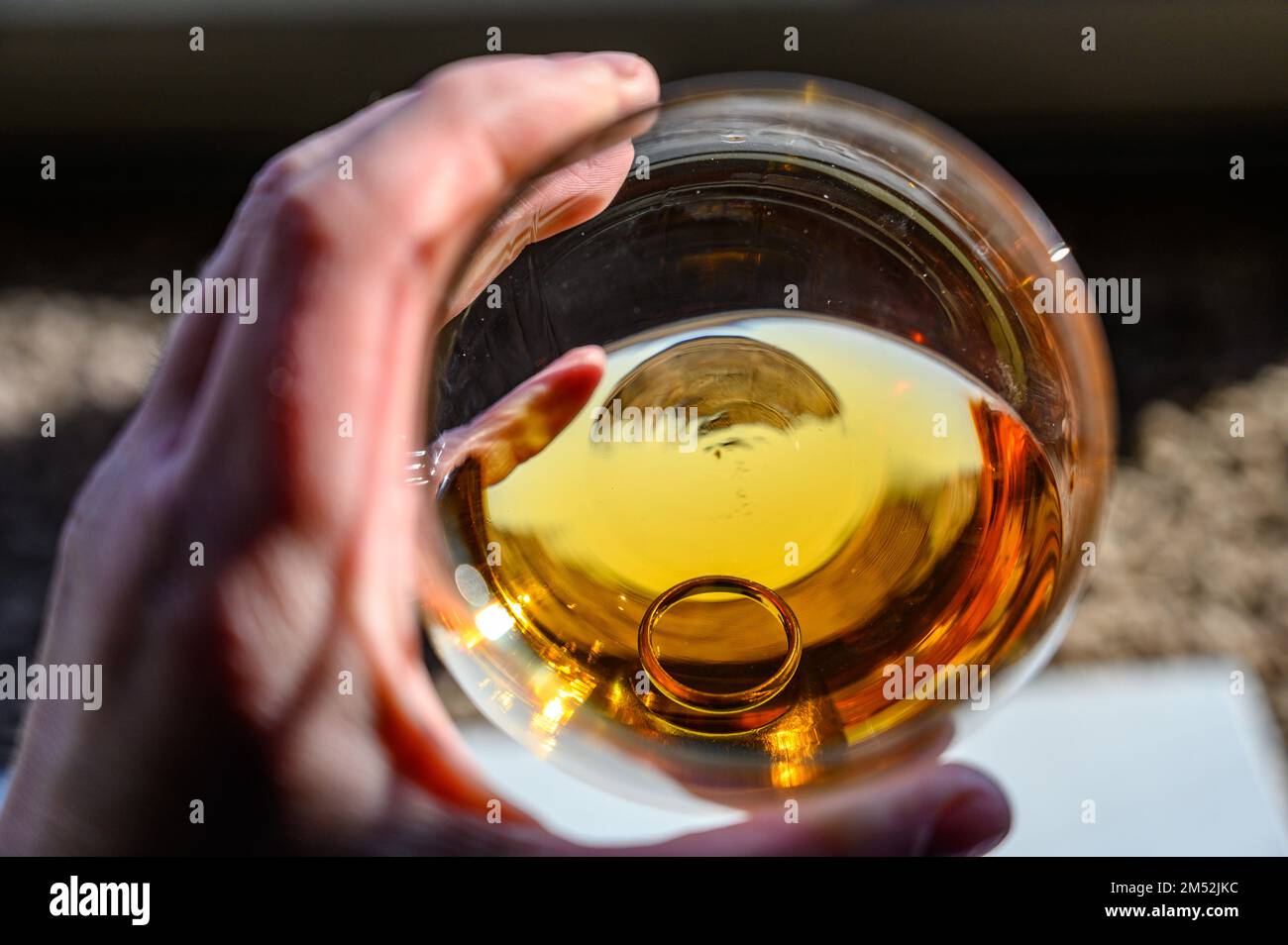 Caucasian hand holding a glass of amber colored liquid with a wedding ...