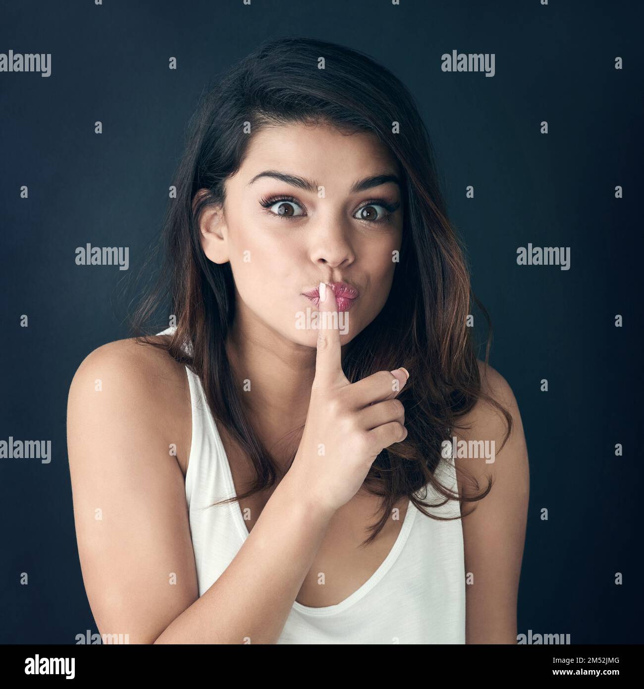 Ask no questions. Studio shot of a beautiful young woman posing with her finger on her lips ...