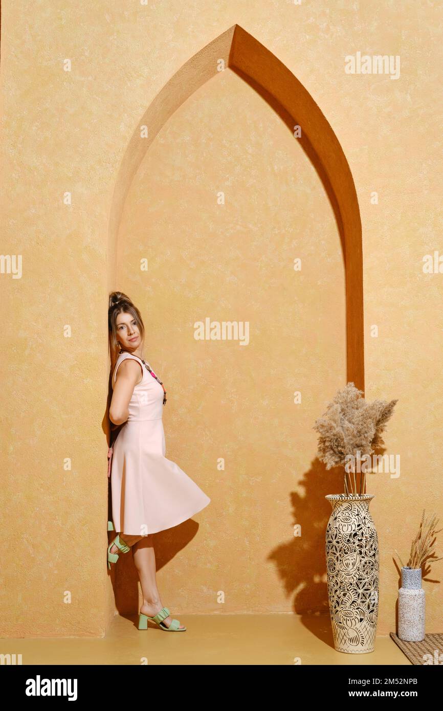 Stylish middle aged woman in peach color dress leaning against oriental ...