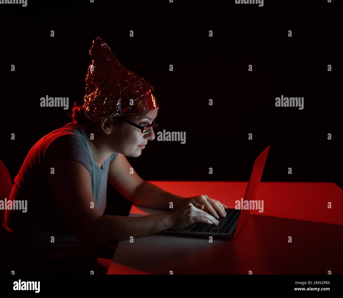 Paranoid caucasian woman typing on a computer wearing a tinfoil cap ...
