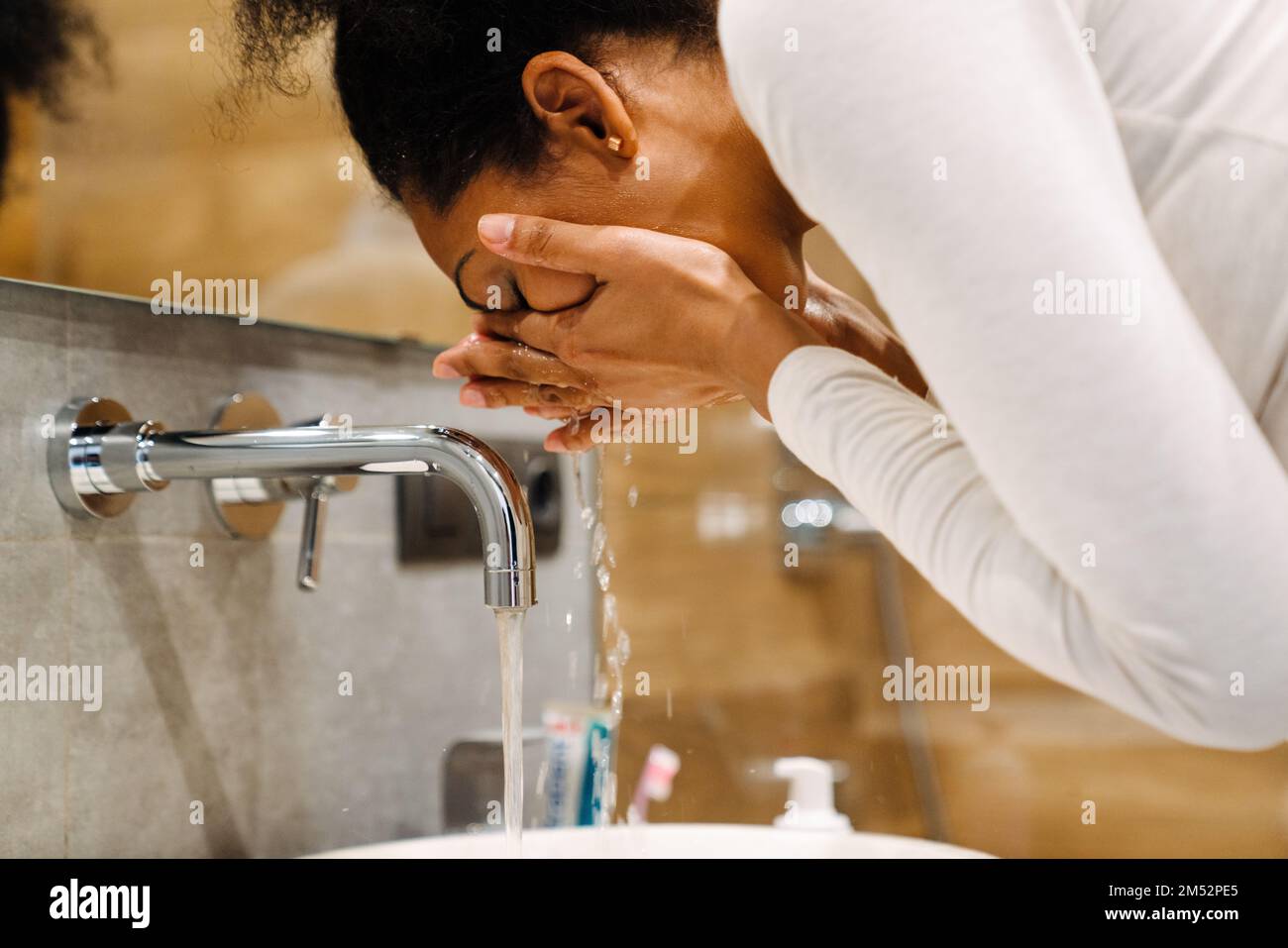 Adult african woman washing her face in bathroom close-up Stock Photo ...
