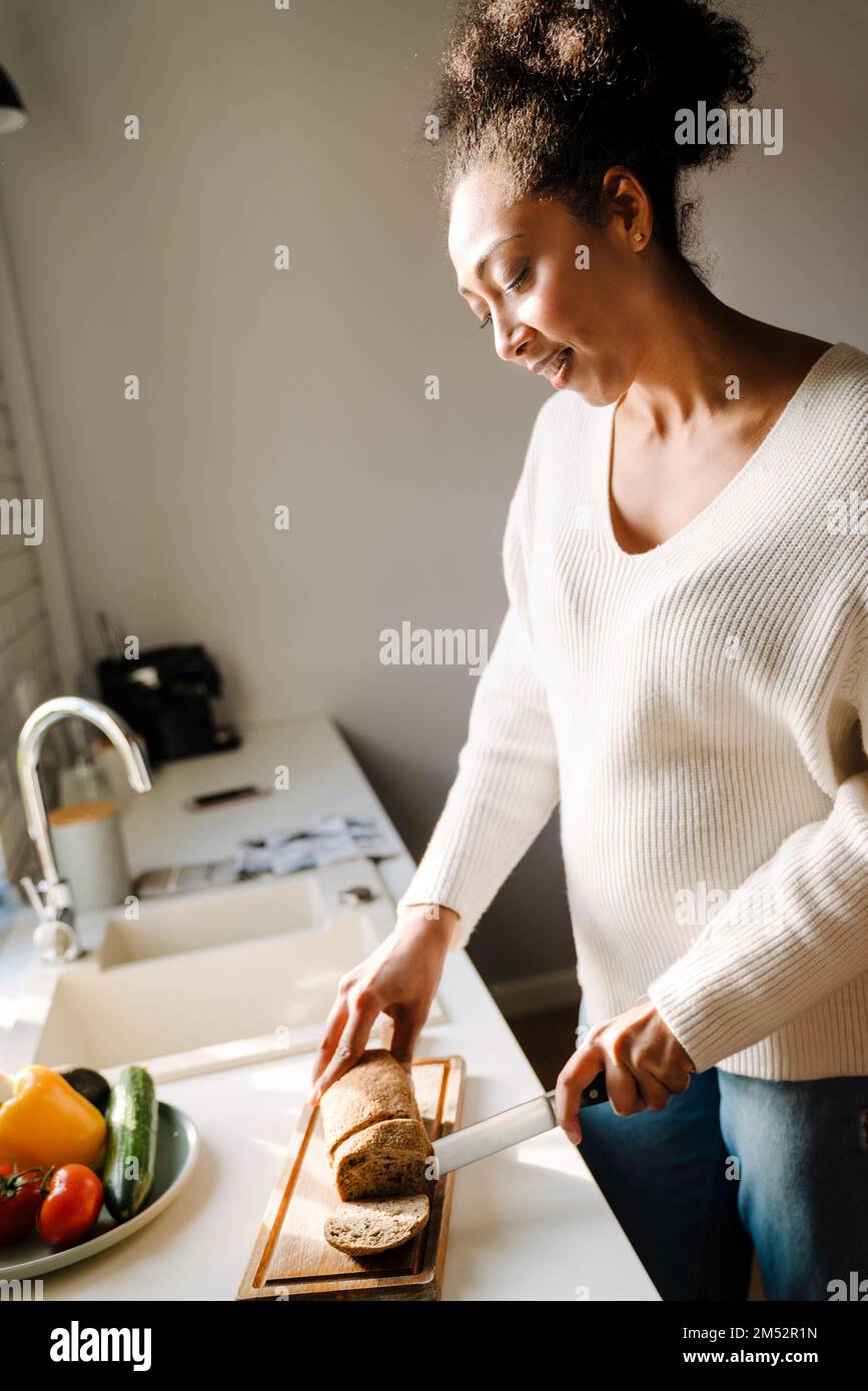 Adult beautiful smiling african pregnant woman cutting bread in cozy kitchen at home Stock Photo ...