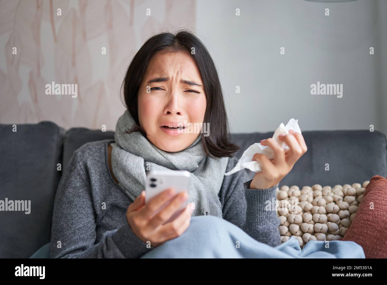 Asian girl with influenza, sits at home, cries and looks upset, holds ...